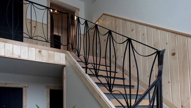 Uma escadaria com guarda-corpo de metal preto, degraus de madeira e um vaso de planta na base.