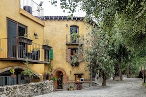 Um edifício com fachada de pedra, várias varandas com plantas e uma rua de paralelepípedos.