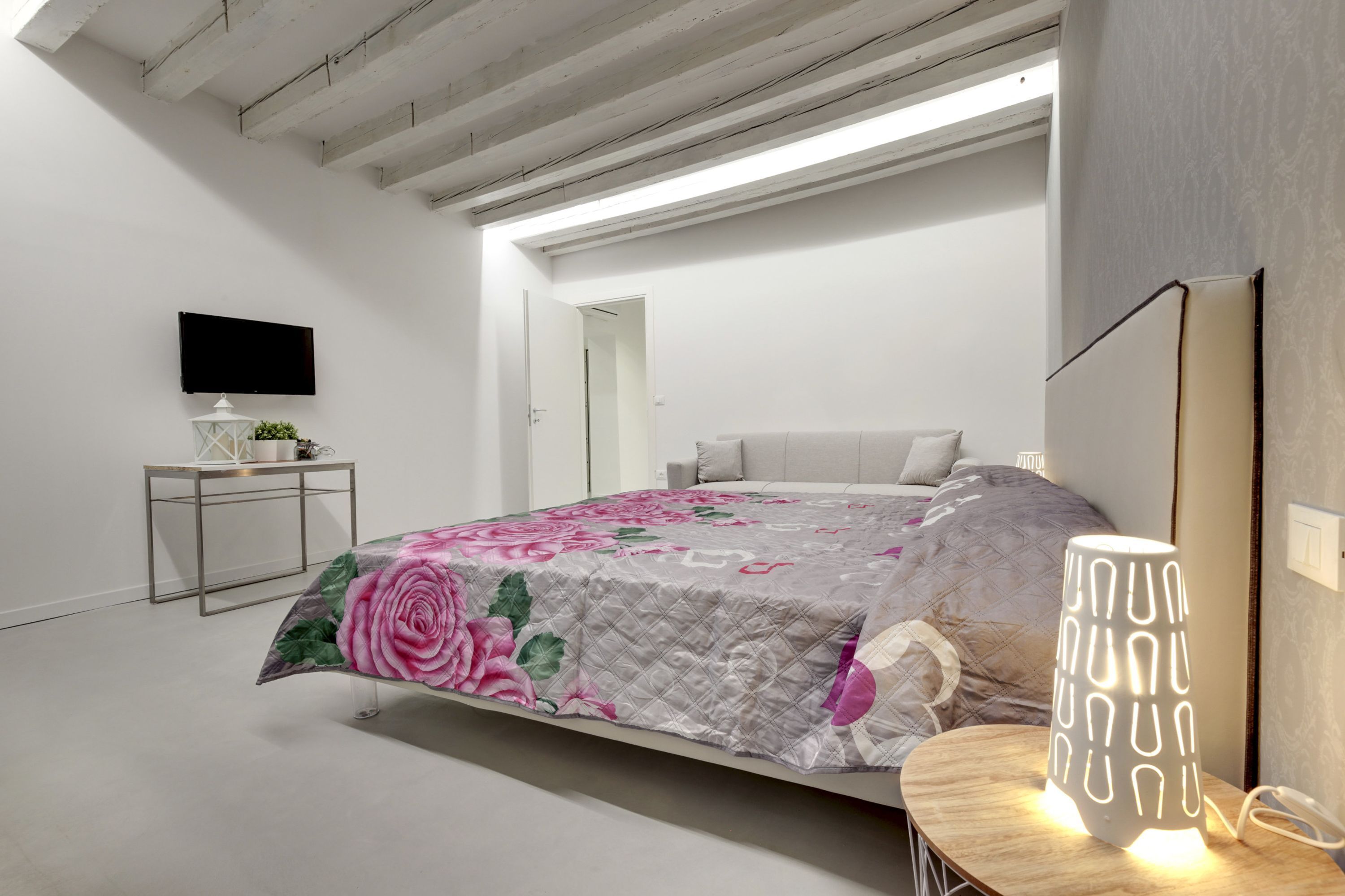 Quarto moderno com cama, mesa de cabeceira, abajur e televisão de tela plana na parede.
