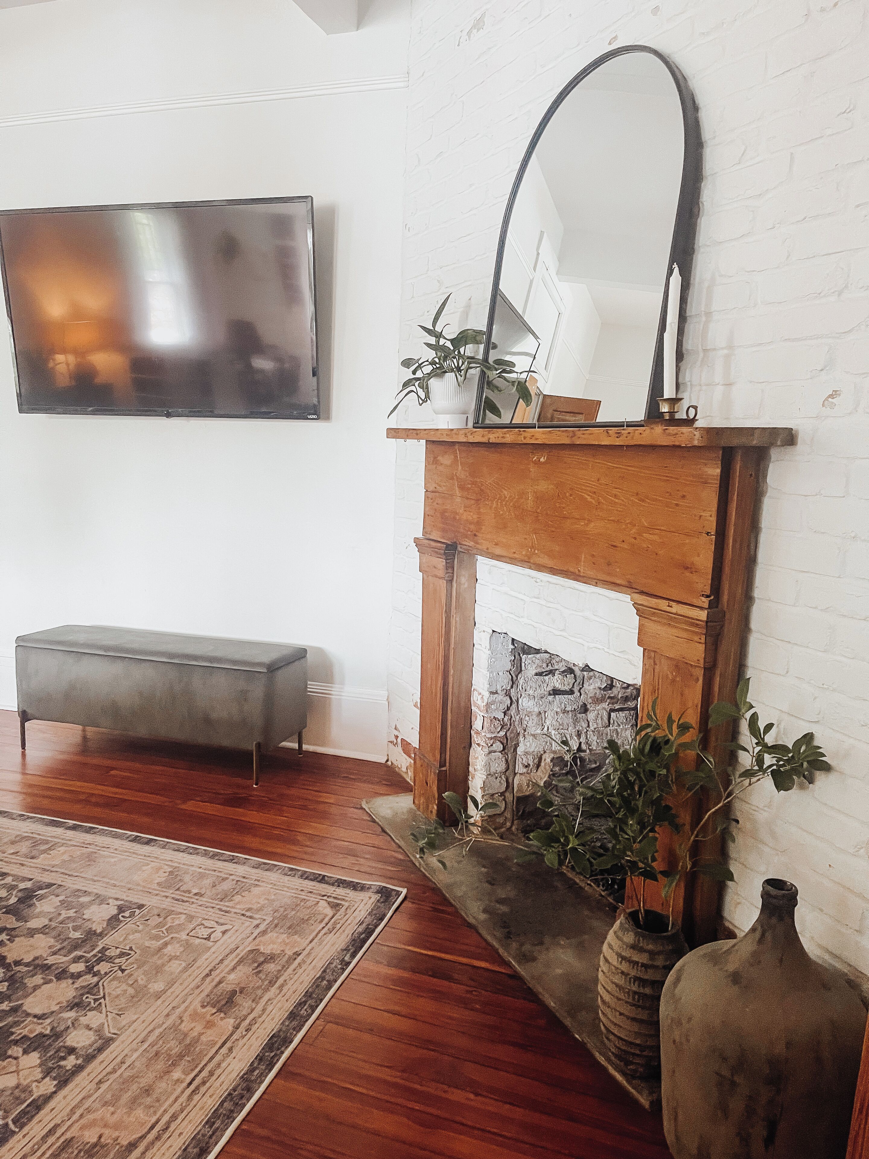 Uma sala de estar com lareira, um banco, uma TV na parede e um tapete rústico.