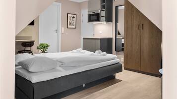 Quarto estilo loft moderno, com cama, escrivaninha e cozinha compacta.