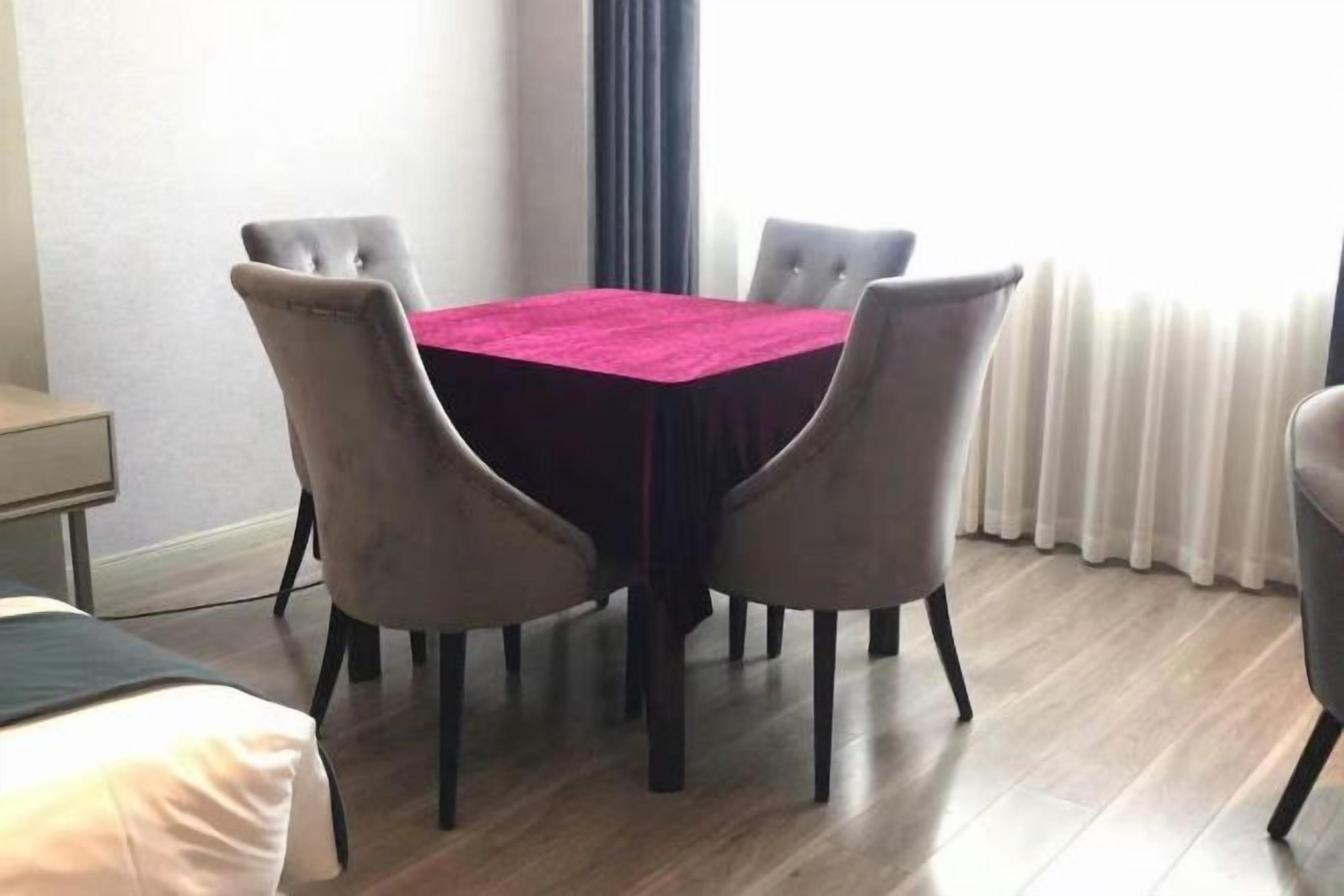 Uma sala de jantar com uma mesa coberta por toalha vermelha, rodeada por quatro cadeiras estofadas.