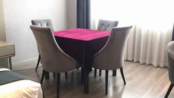 Uma sala de jantar com uma mesa coberta por toalha vermelha, rodeada por quatro cadeiras estofadas.