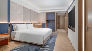 Quarto de hotel moderno com uma cama grande, mesa de cabeceira, armário e banheiro visível através de uma porta aberta.