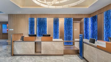 Uma área de recepção de hotel moderna, com um balcão de mármore, um visor digital e um painel de parede em mármore azul.
