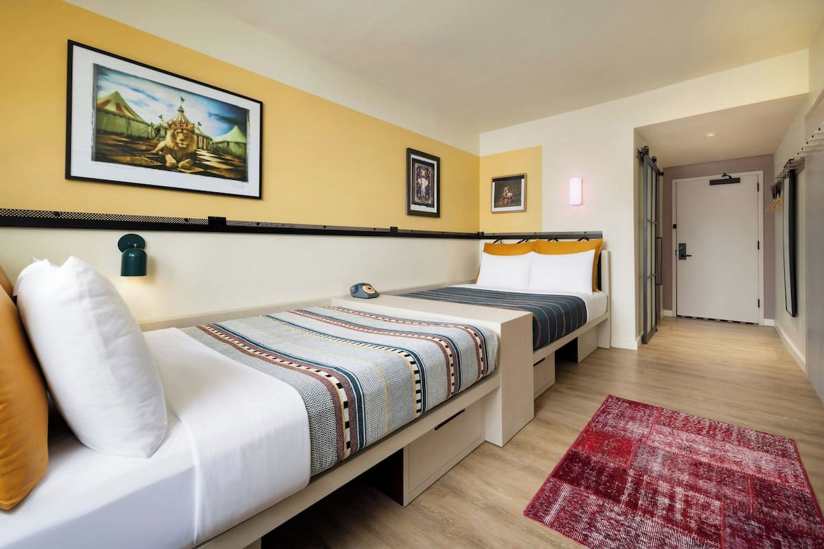 Quarto de hotel com duas camas de solteiro, um tapete vermelho e um quadro na parede.