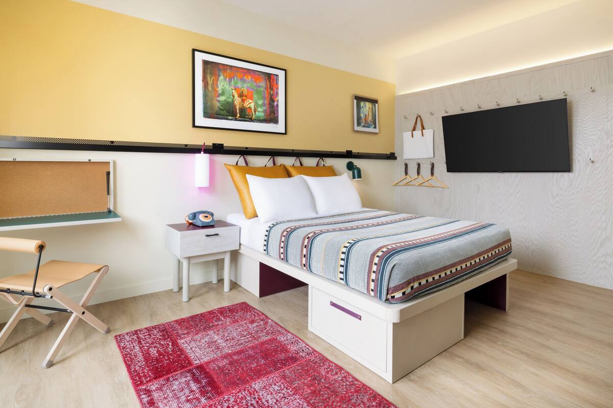 Quarto moderno com cama, mesa de cabeceira e tapete vermelho.