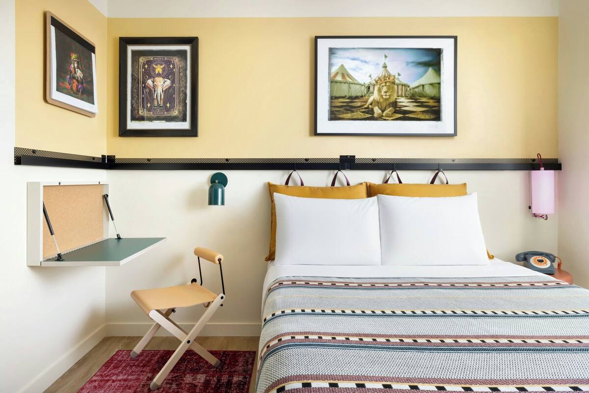 Quarto com cama, cadeira, prateleira e quadros na parede.