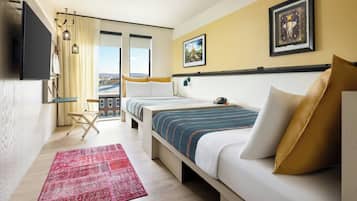 Quarto de hotel com uma cama grande, televisão na parede, tapete vermelho e janela com vista para edifícios.