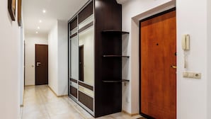 Um corredor com porta de madeira, telefone e prateleira na parede.