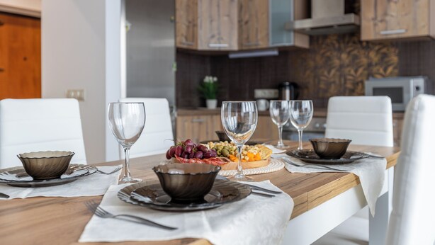 Uma mesa de jantar posta com tigelas, pratos, talheres e copos, com uma composição de frutas e nozes no centro.