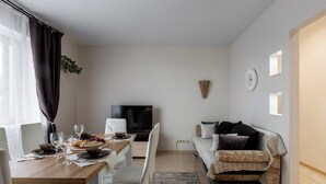 Uma sala de estar moderna com área de jantar, um sofá, uma TV e um relógio na parede.