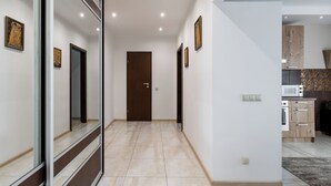 Corredor moderno com porta de madeira, espelho e área de cozinha com armários e eletrodomésticos de madeira.