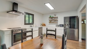 Cozinha moderna com armários brancos, mesa de jantar de madeira e eletrodomésticos de aço inoxidável.