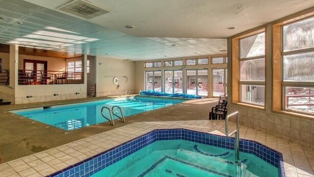 Piscina interna com área de hidromassagem separada, grandes janelas e espaço de estar com mesas e cadeiras.