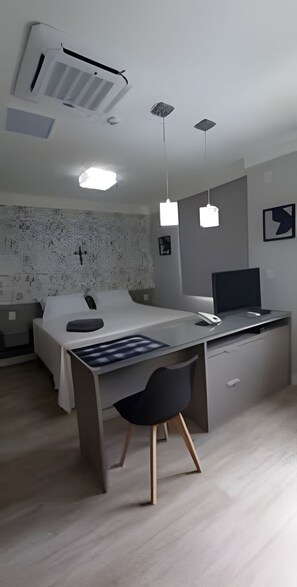 Quarto moderno com cama, escrivaninha e cadeira. Há uma TV na escrivaninha e uma cruz na parede.