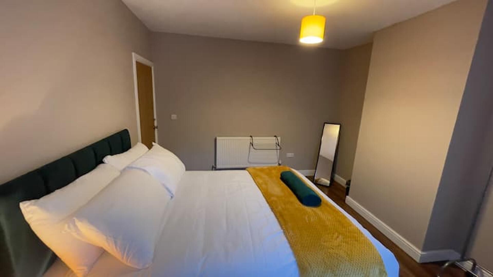 Quarto com cama, radiador, espelho e luminária pendente.