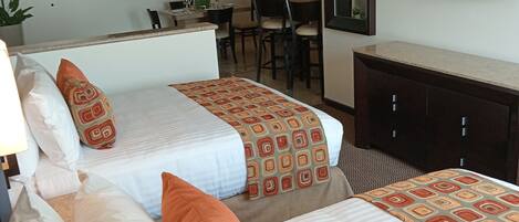 Quarto de hotel com duas camas, uma escrivaninha, uma cadeira, uma TV e um espelho.