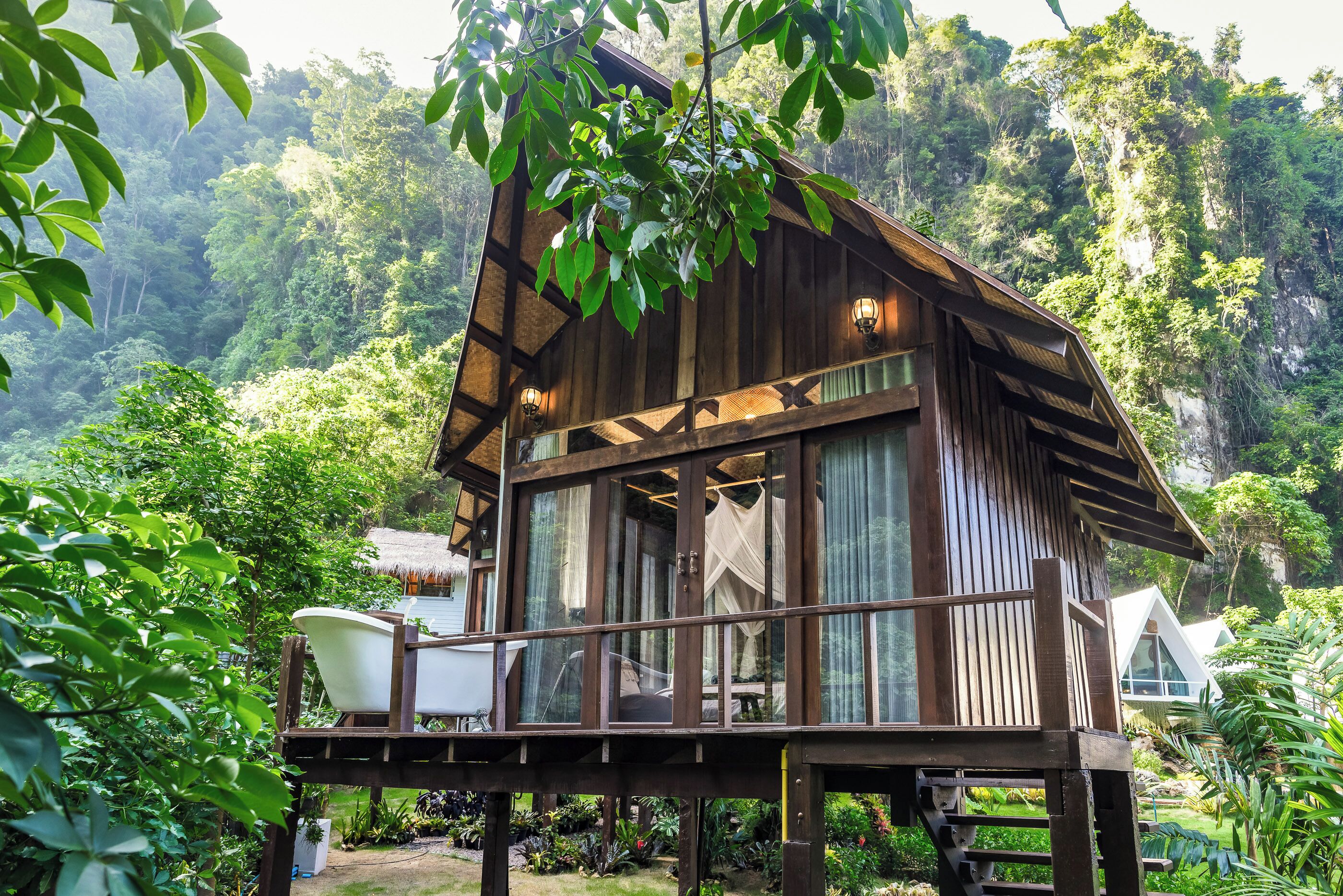 Uma cabana de madeira com varanda, rodeada por vegetação exuberante e um cenário montanhoso.