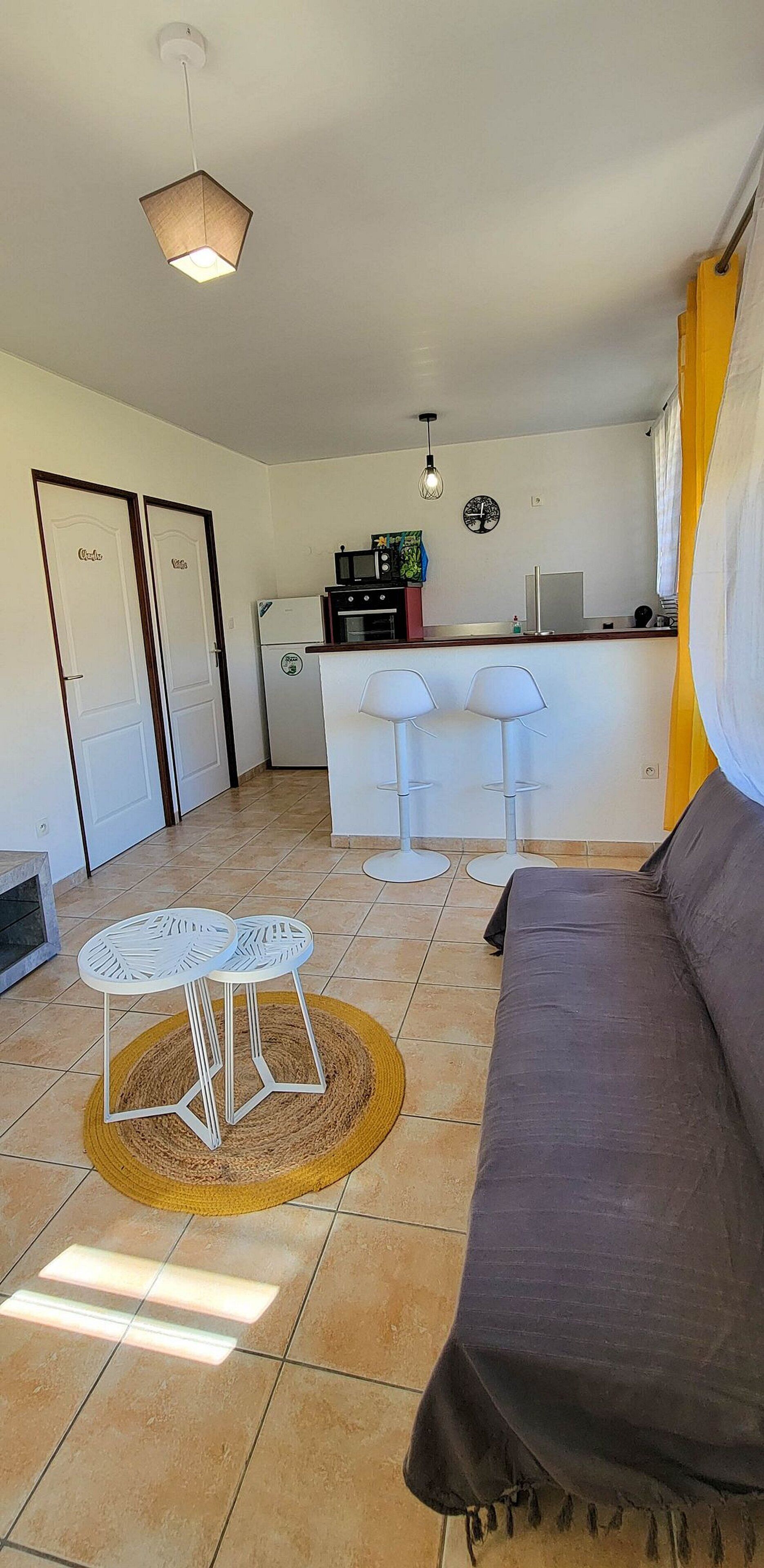 Um espaço compacto para viver, com cozinha compacta, dois bancos brancos, sofá e tapete estampado.