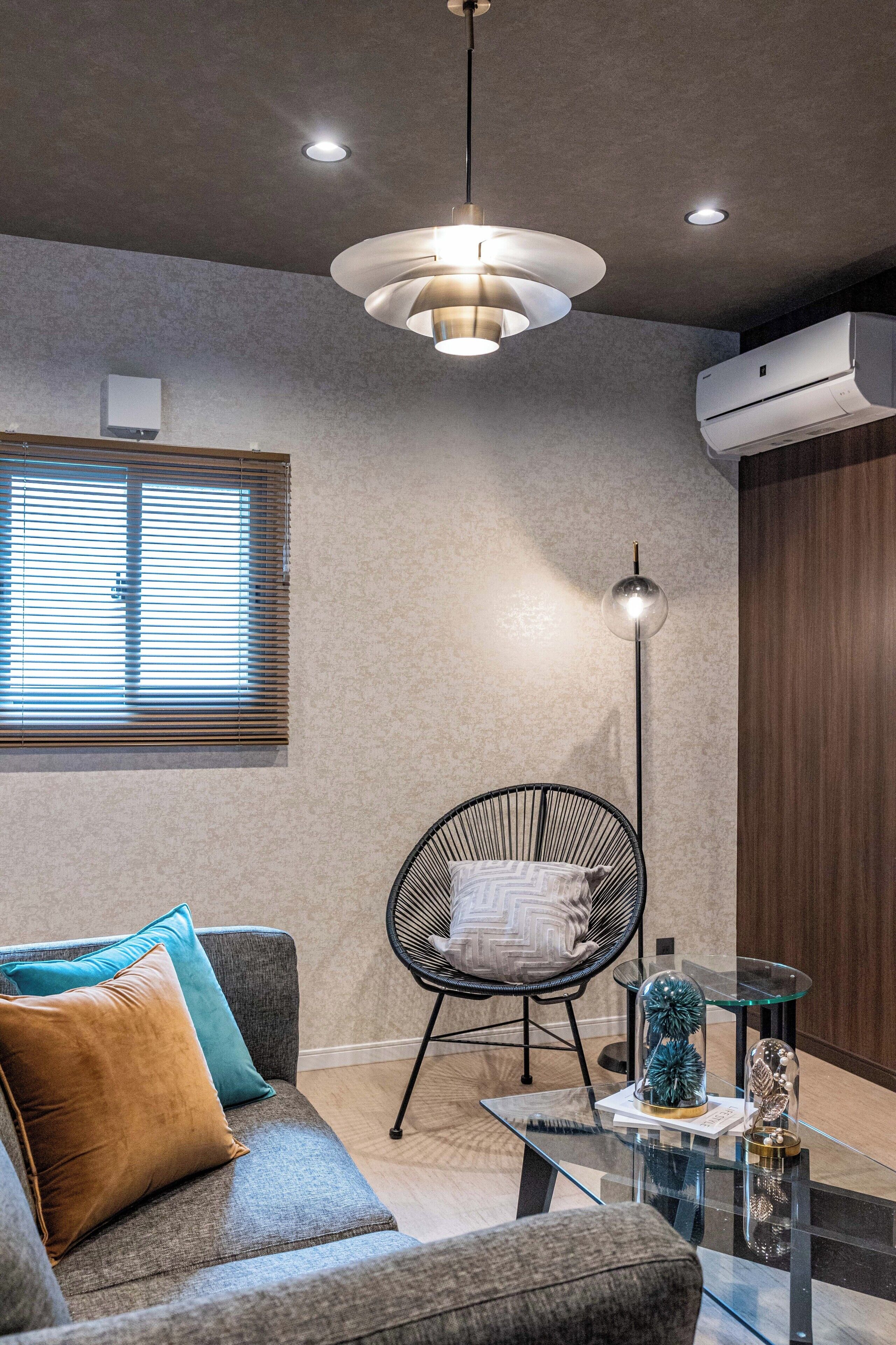 Uma sala de estar moderna com um sofá cinzento, uma cadeira preta, uma mesa de centro de vidro e uma luminária pendente.