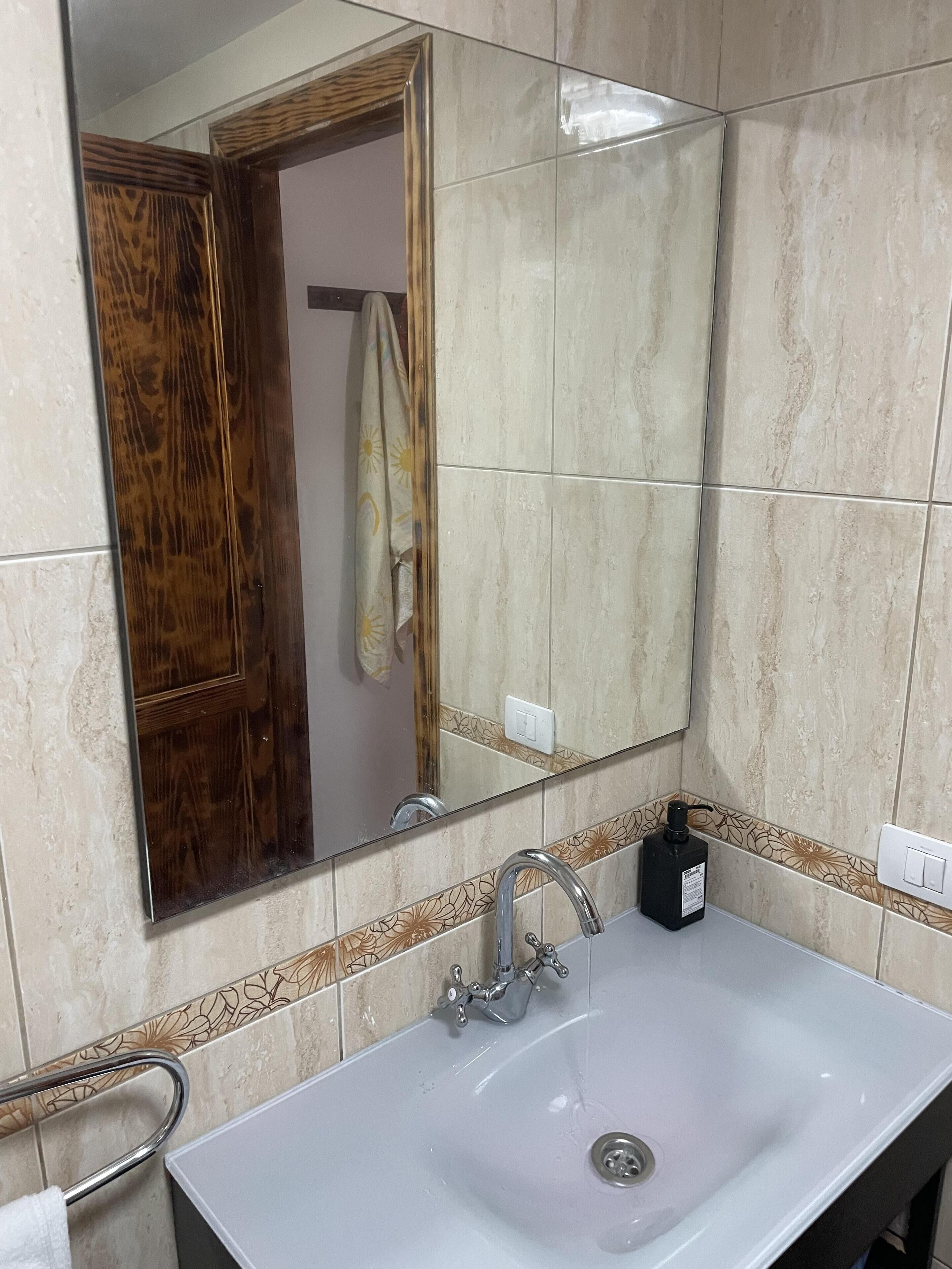 Casa de banho com lavatório branco, espelho e porta de madeira.