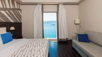 Quarto de hotel com cama, sofá, vista para o mar e janela com cortinas.