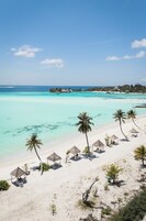 Uma praia com águas turquesa cristalinas, palmeiras e cabanas de praia.