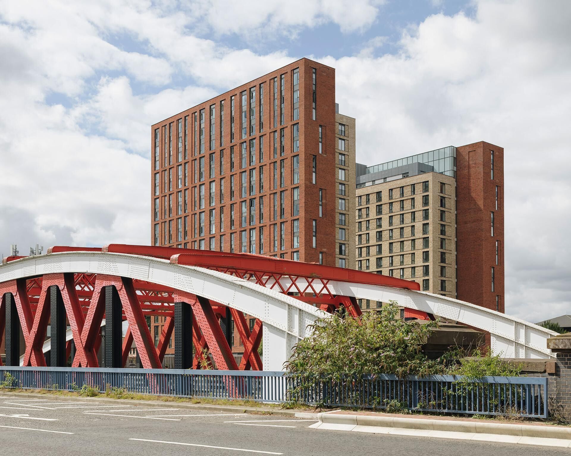 Uma ponte de metal vermelha com um arco branco sobre uma estrada, com edifícios altos ao fundo.