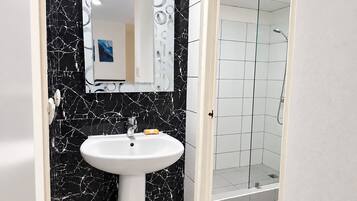 Casa de banho com lavatório pedestal branco, espelho em cima e cabine de duche em vidro.