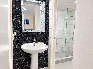 Casa de banho com lavatório pedestal branco, espelho em cima e cabine de duche em vidro.