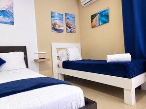 Quarto de hotel com duas camas, decoração azul e branca e obras de arte nas paredes.