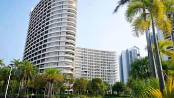 Um hotel com várias andares e fachada curva, rodeado por palmeiras e um céu claro.