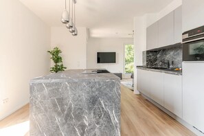 Uma cozinha moderna com ilha de mármore, eletrodomésticos de aço inoxidável e uma televisão de tela plana.