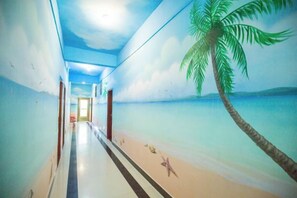 Corredor com um mural de praia, palmeira e vista para o oceano.
