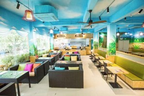 Restaurante interno com pé direito alto, ventiladores no teto e vista para o exterior.