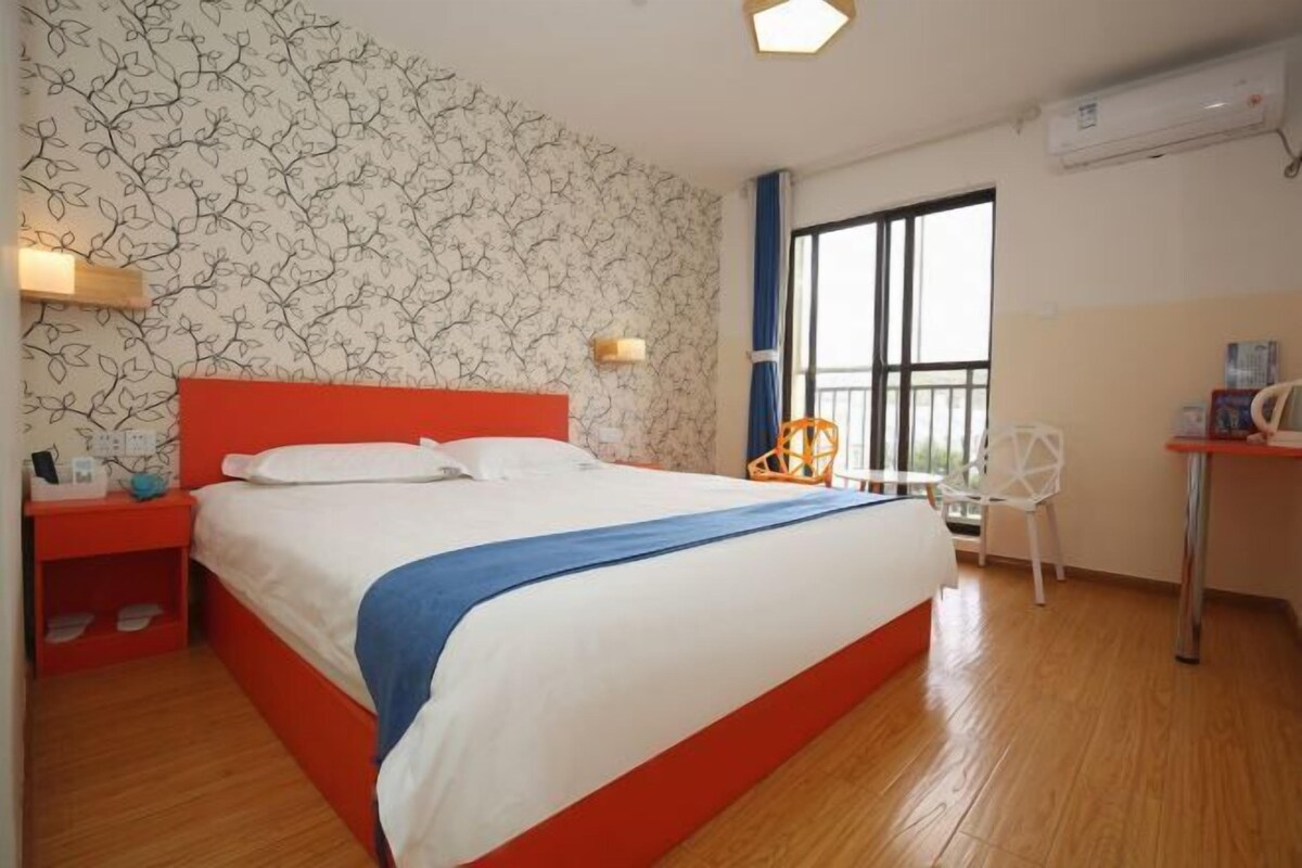 Quarto de hotel com cama, escrivaninha, cadeira e janela.
