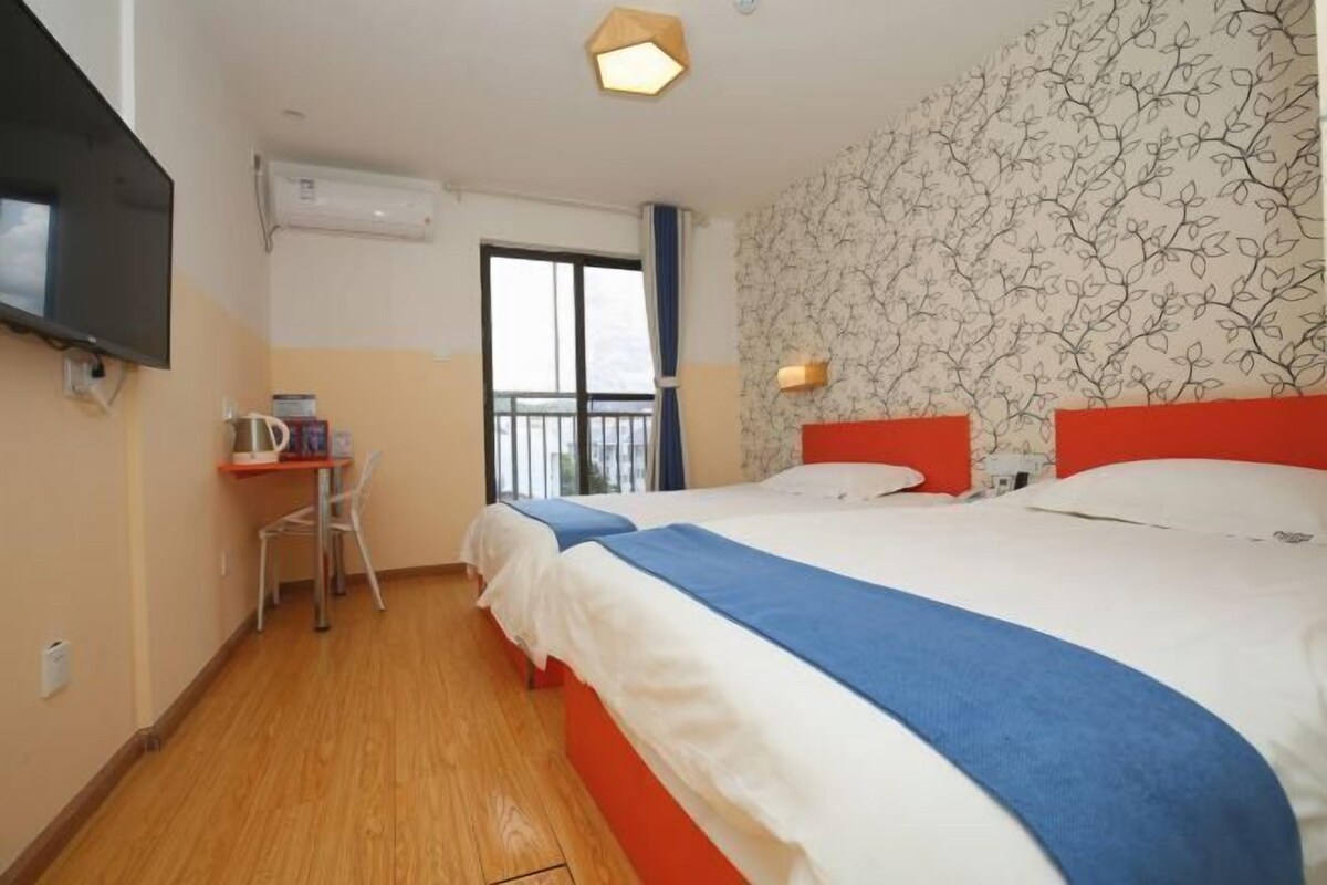 Quarto de hotel com duas camas, uma escrivaninha com cadeira, uma televisão e uma janela com vista.