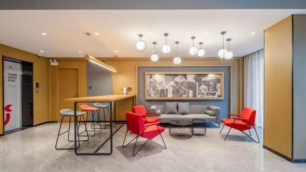 Um hall de hotel moderno com uma mesa de recepção, um sofá, cadeiras vermelhas e uma mesa de centro.