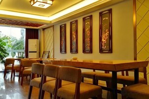 Uma sala de jantar de hotel com uma longa mesa de madeira, várias cadeiras e obras de arte emolduradas na parede.