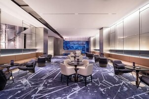 Um hall de hotel moderno com piso de mármore, mesas redondas e assentos confortáveis.
