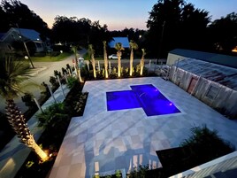 Uma piscina com design geométrico em mosaicos, cercada por palmeiras e um muro.