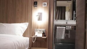 Quarto de hotel com cabeceira de madeira, telefone ao lado da cama e porta de vidro do chuveiro.