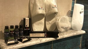 Uma bancada de banheiro com produtos de higiene Star Inn, kit de higiene bucal, chinelos e um dispensador de sabonete.