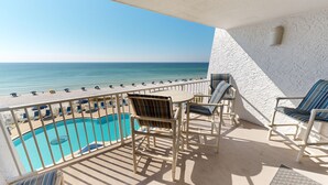 Uma varanda com piscina, cadeiras e vista para a praia e oceano.
