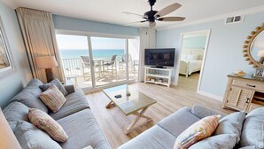 Uma sala de estar moderna com um conjunto de sofás, uma mesa de centro, uma TV e uma varanda com vista para o mar.
