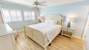 Quarto com cama, duas mesas de cabeceira, ventoinha no teto e janela com persianas.