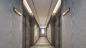 Um corredor comprido e estreito com piso estampado, paredes com painéis texturizados e iluminação no teto.