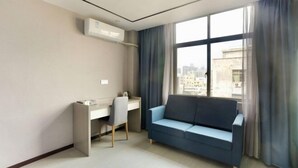 Quarto de hotel moderno com escrivaninha, sofá azul e uma grande janela com vista para a cidade.