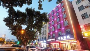 Hotel com vários andares, sinalização iluminada, carros estacionados e árvores ao fundo.
